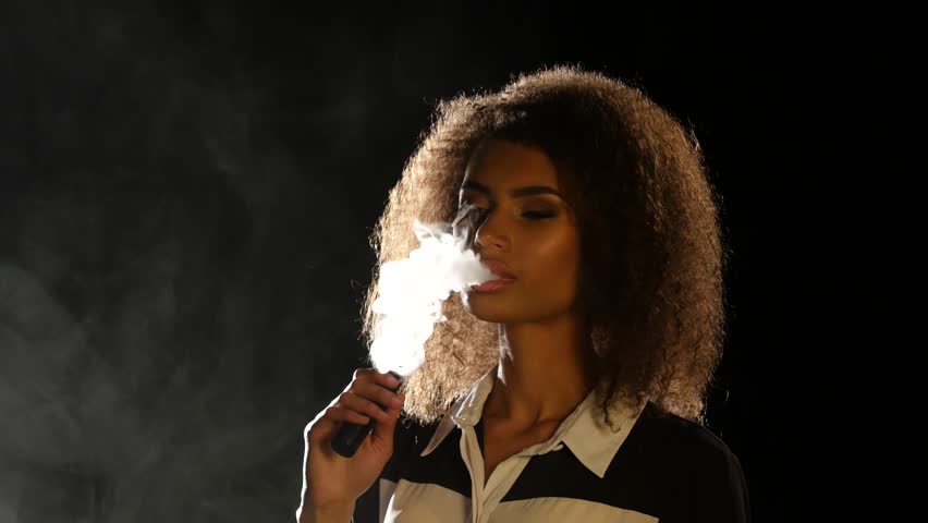 African American Girl Smokes An Electronic Cigarette In An Empty Room Black Background Slow