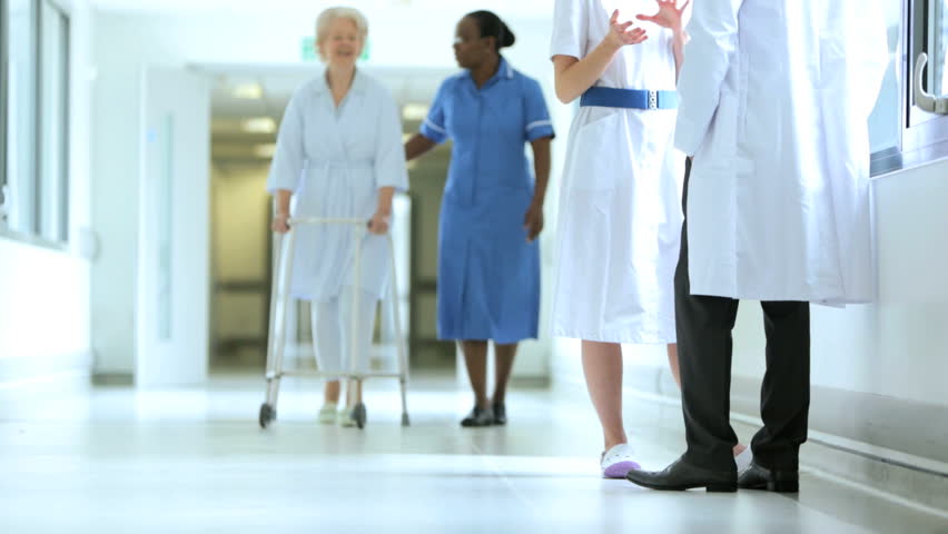 Elderly Patient Walking Down Hospital Corridor With Help Of A Walker ...